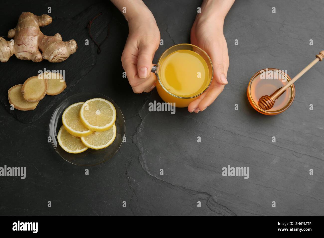 Woman holding cup of immunity boosting drink at dark table with ...