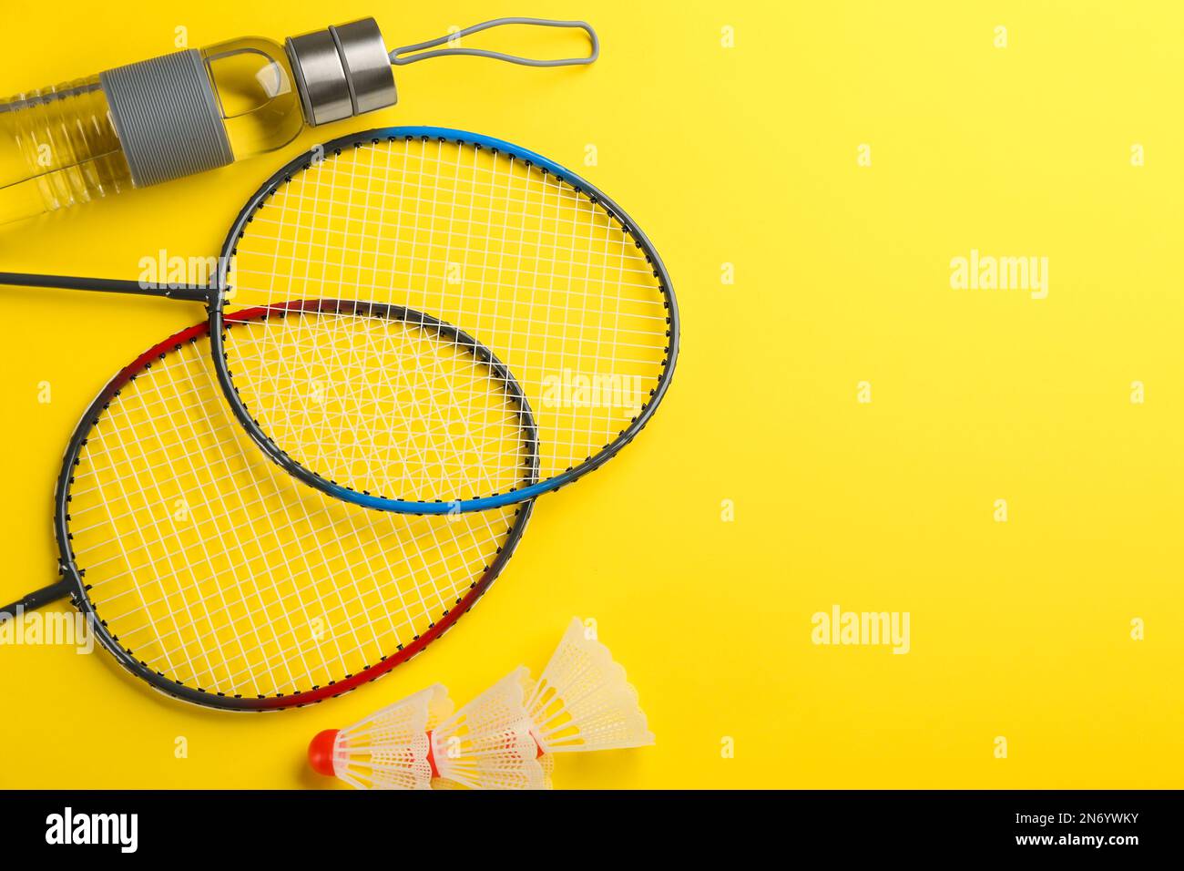 Badminton rackets, shuttlecocks and bottle yellow background, flat lay ...