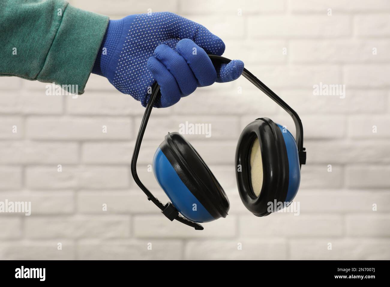 Worker holding safety headphones against white brick wall, closeup ...