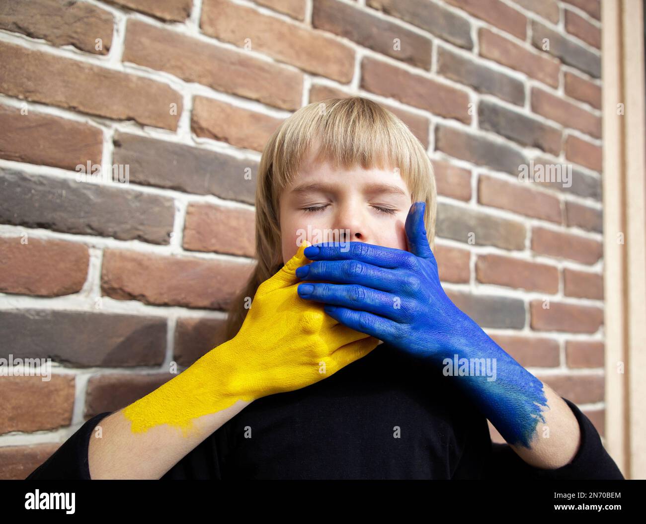 face of child with closed eyes, covered with hands painted in colors of ...