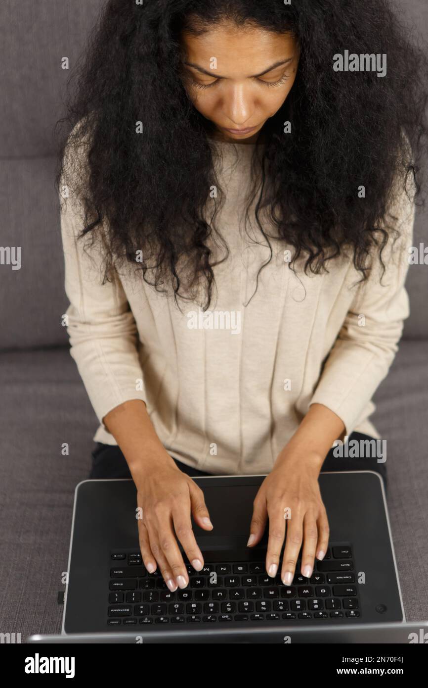 Young black woman working on laptop computer in overhead photo. Focused ...