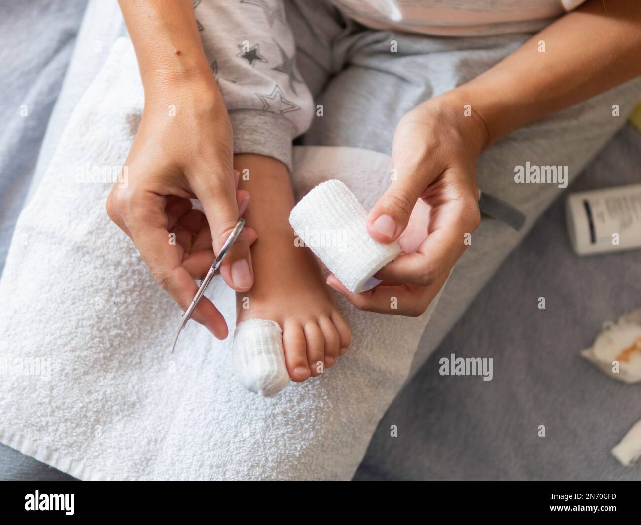 Mother bandages her child's big toe. Close-up photo of kid's foot with ...