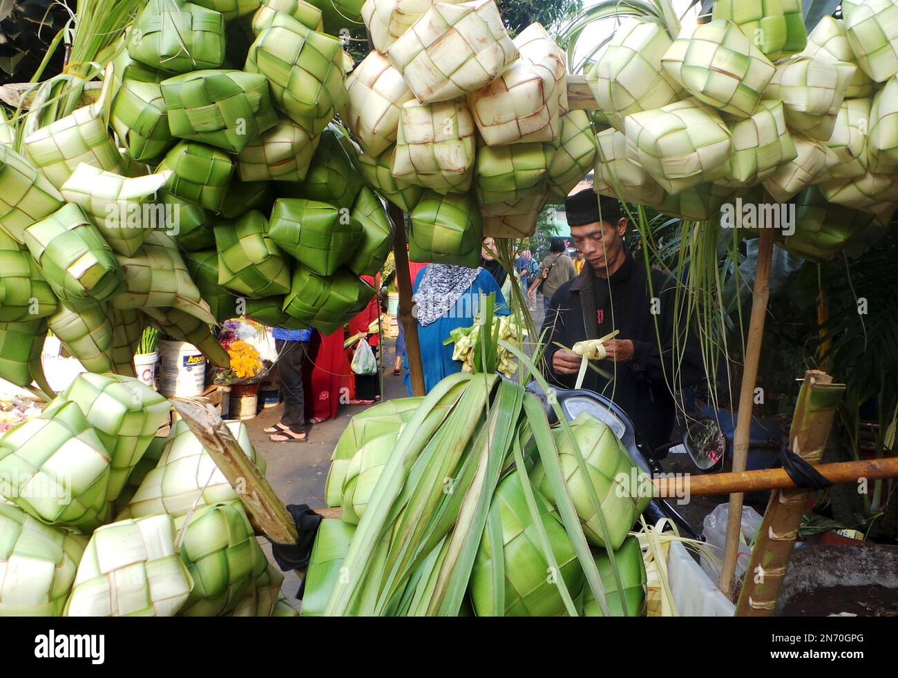 A vendor weaves palm leaves into " ketupat," a square pouch that will ...