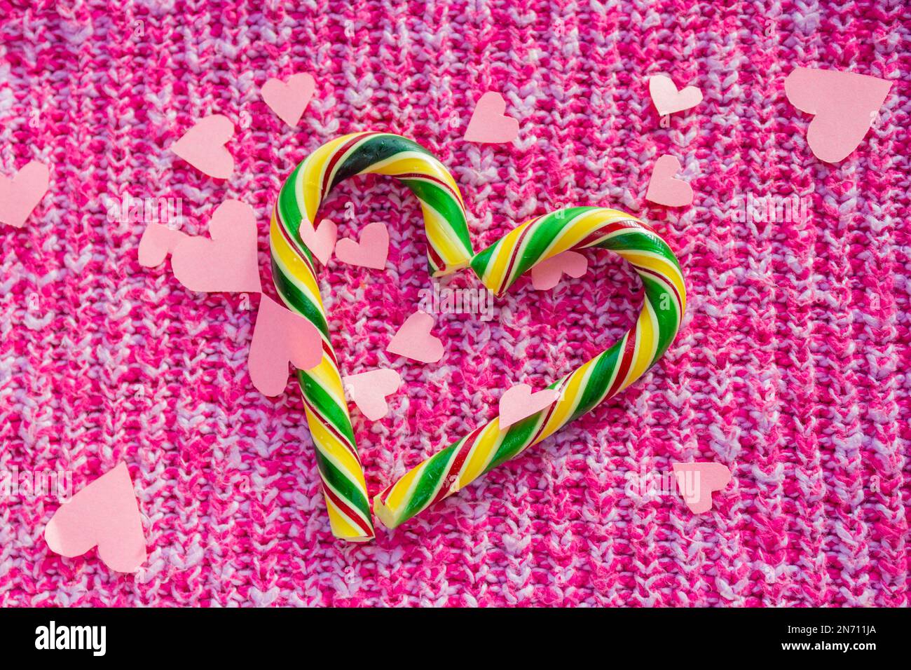 Candy cane sweets forming a heart shape on a pink background with small ...