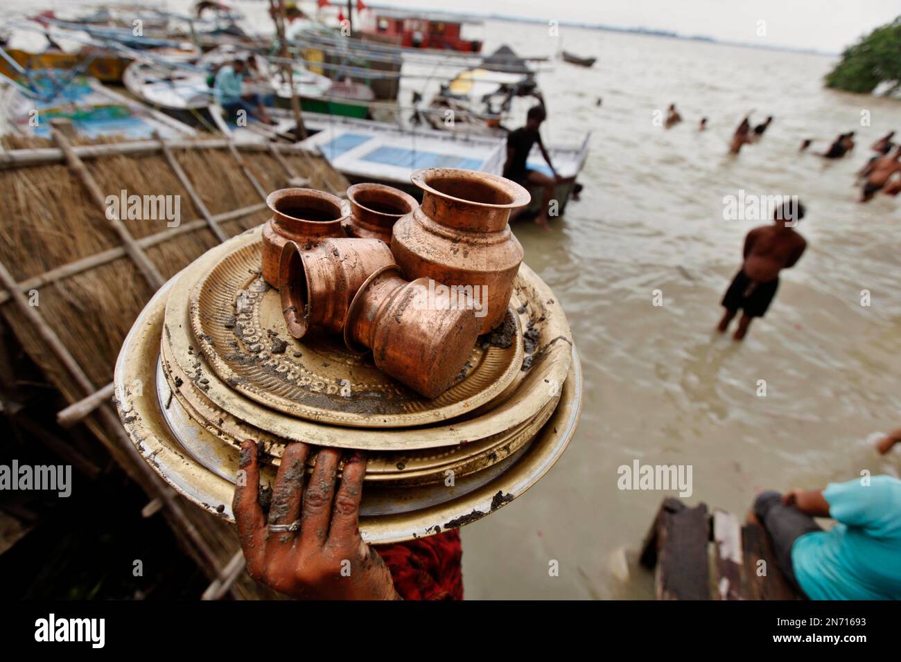An Indian devotee carries dirty vessels as others take bath in the ...