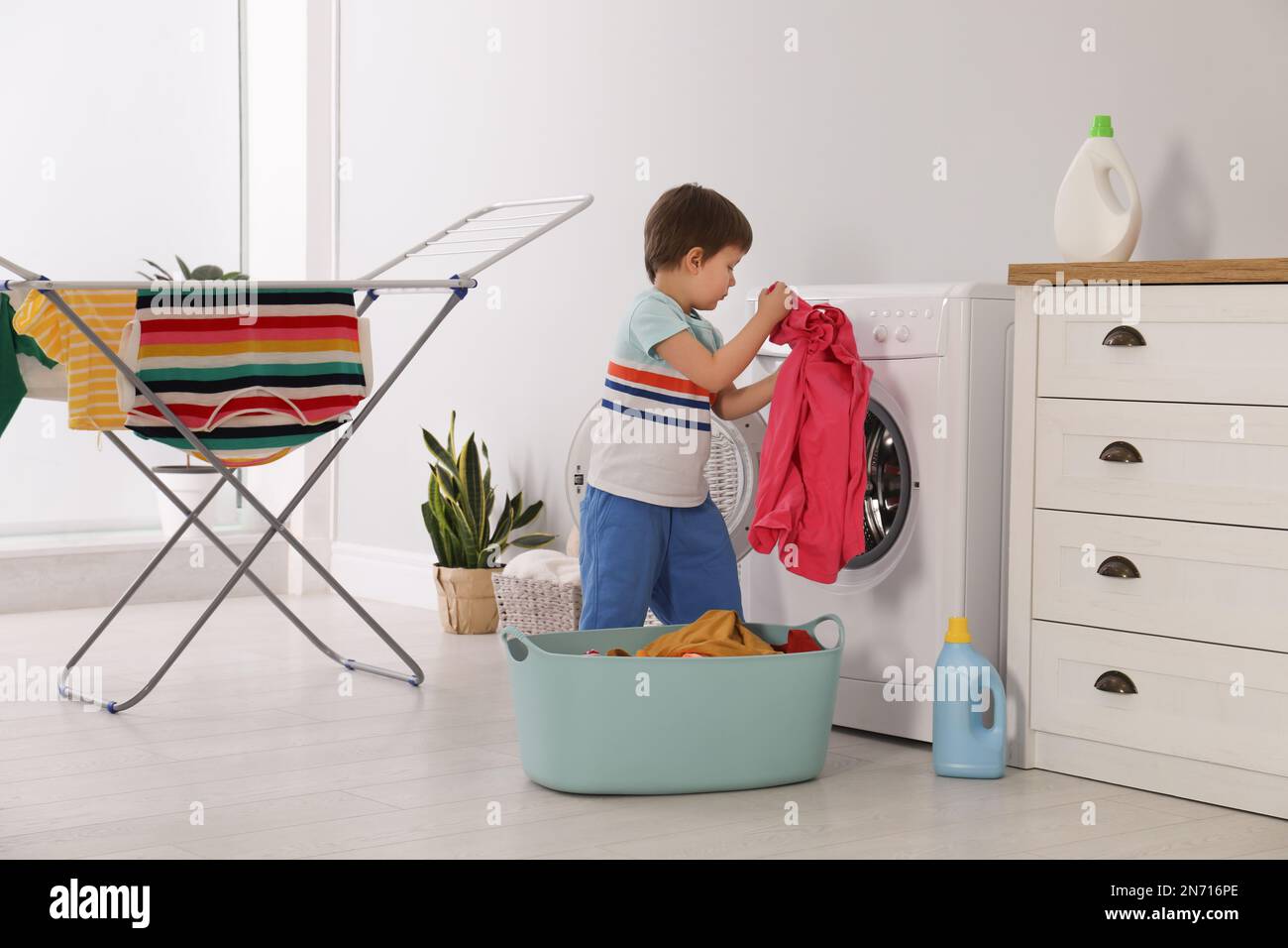 Cute little boy with laundry near washing machine and clothes drying ...