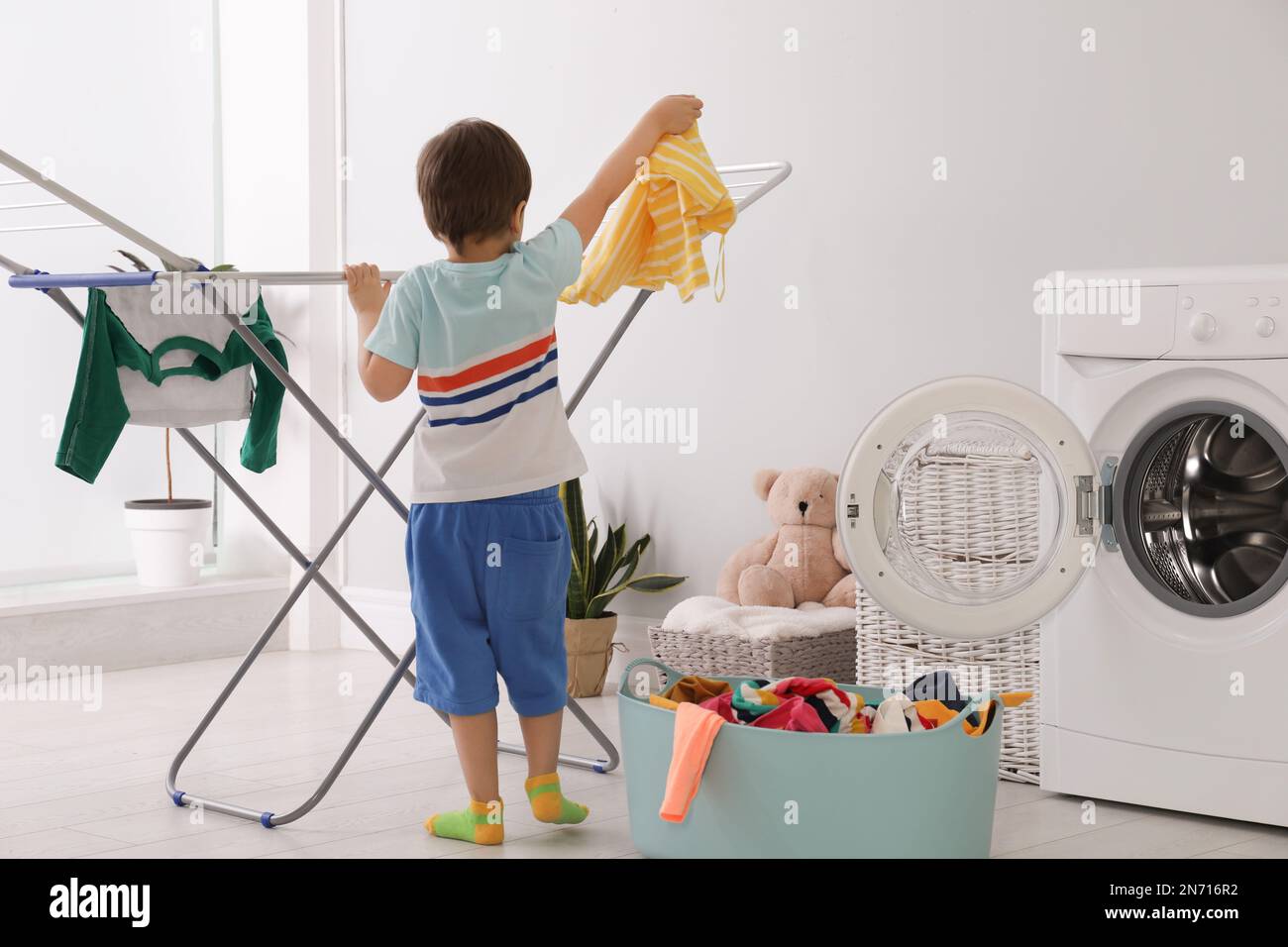 Cute little boy hanging laundry onto clothes drying rack indoors, back ...