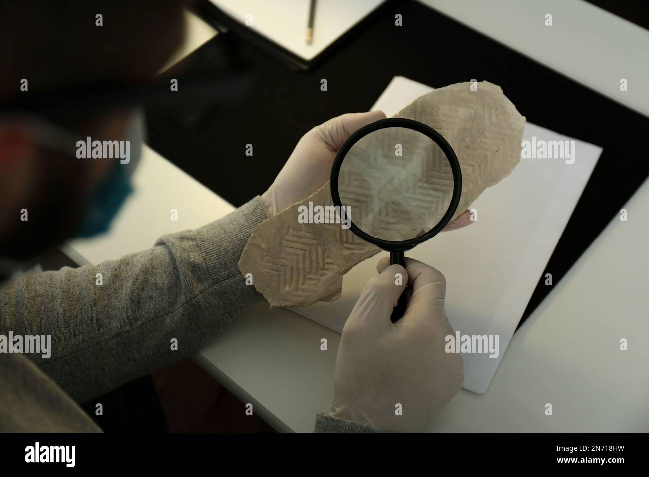 Detective with magnifying glass examining shoe sole print at table ...
