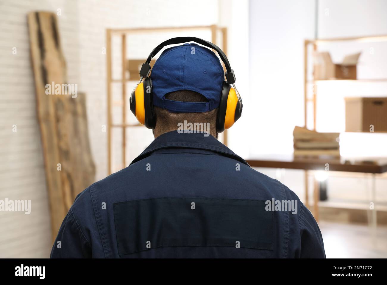 Worker wearing safety headphones indoors, back view. Hearing protection ...