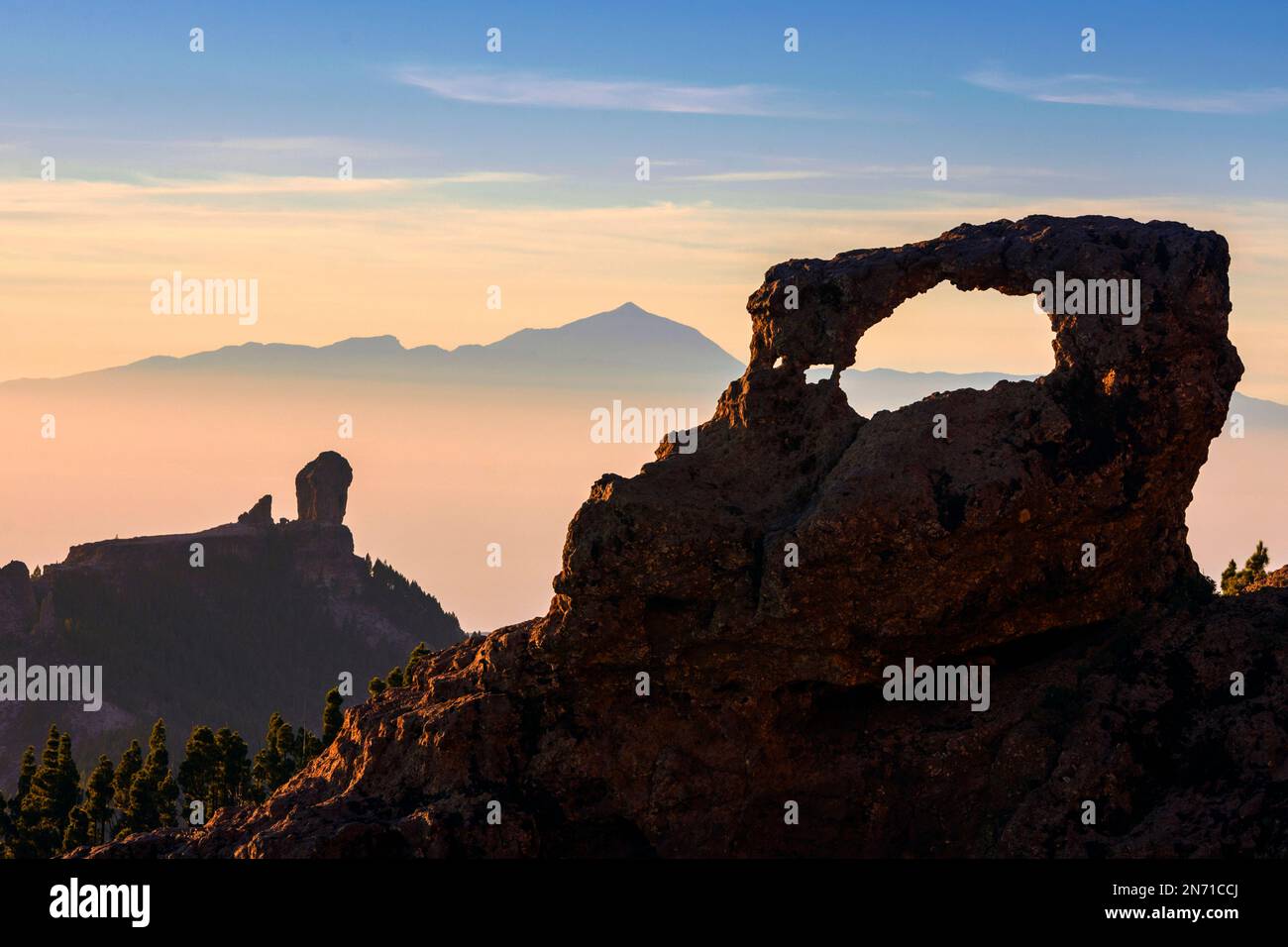 Silhouette of Roque Nublo and natural rock arch at sunset with Mt Teide ...