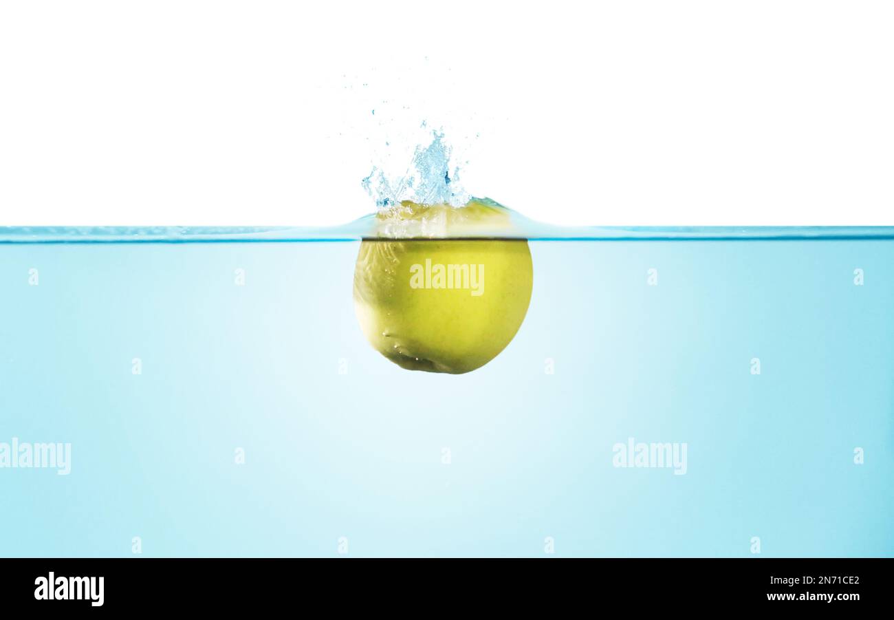 Green apple falling down into clear water against white background ...