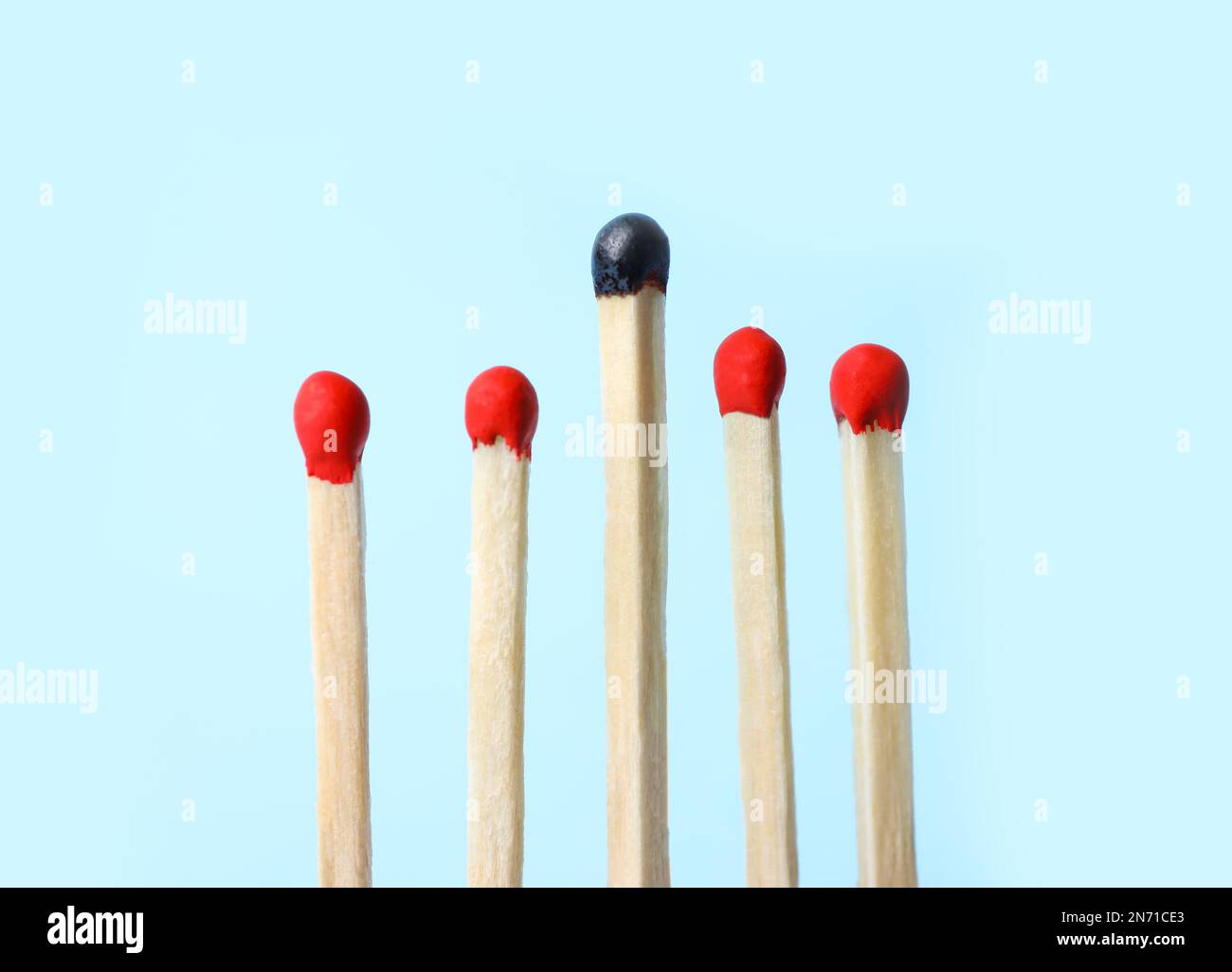 Row of whole matches and burnt one on light blue background. Uniqueness ...