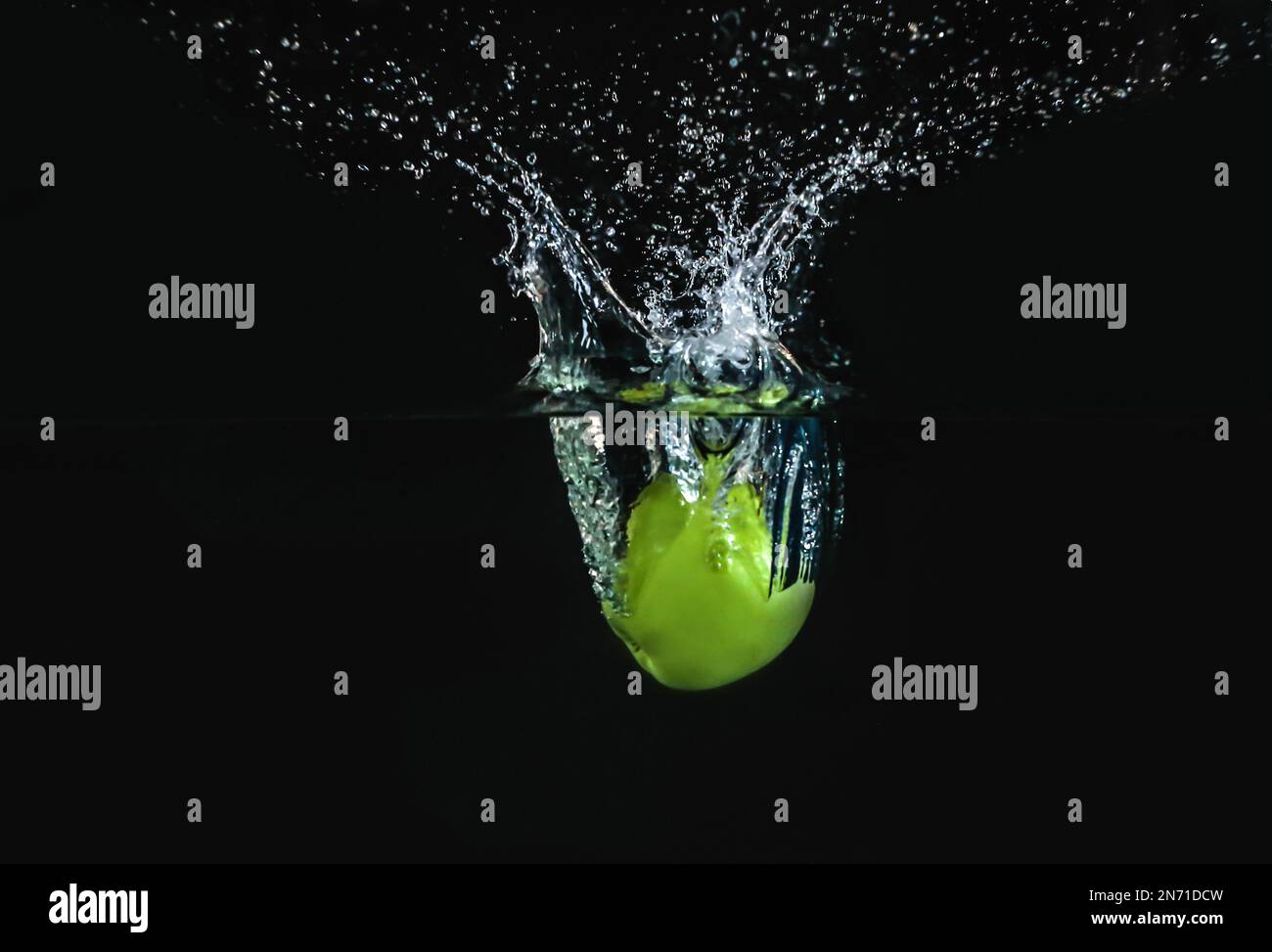 Ripe green apple falling down into clear water with splashes against ...
