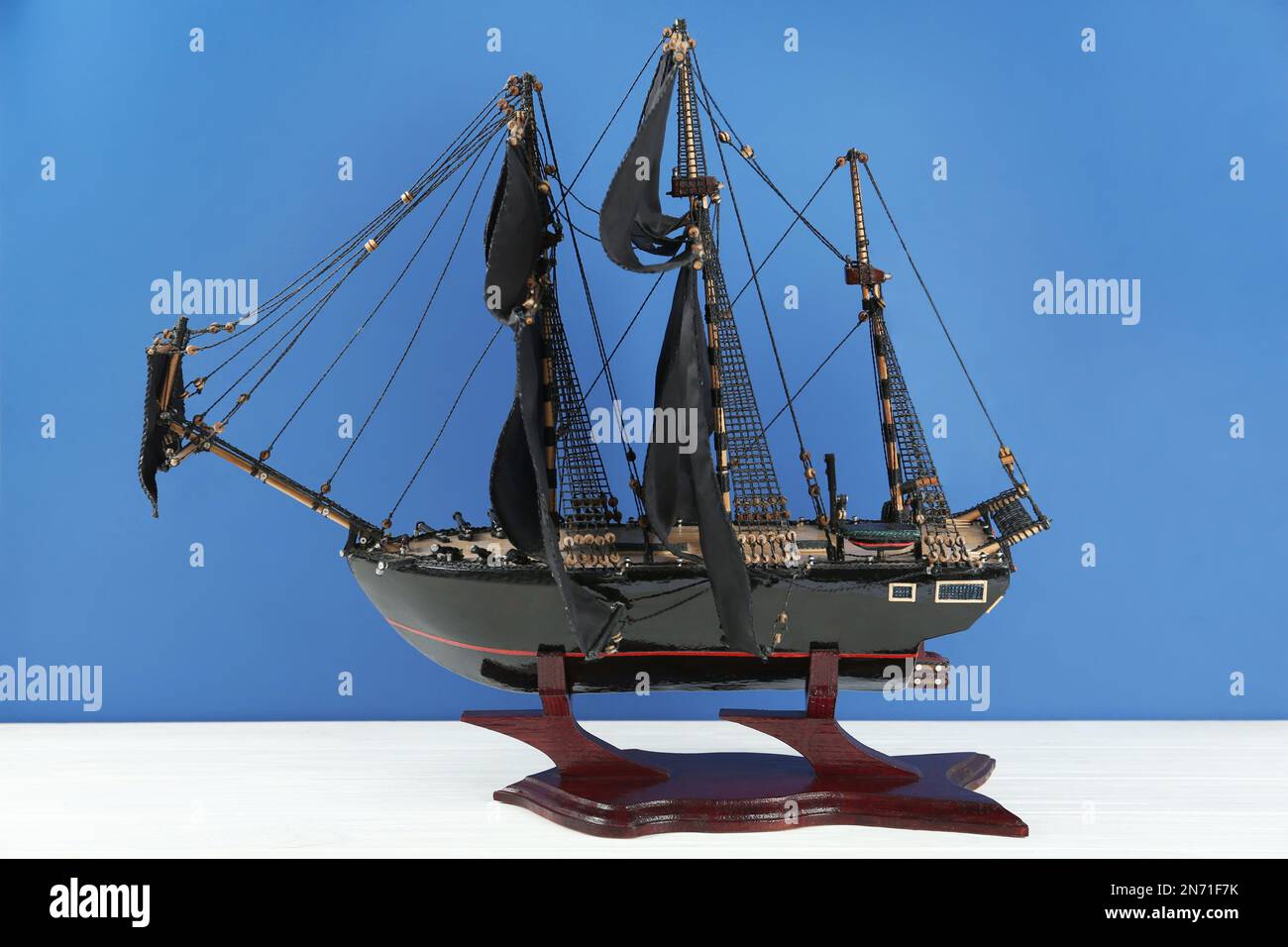 Miniature model of old ship with black sails on white table against ...