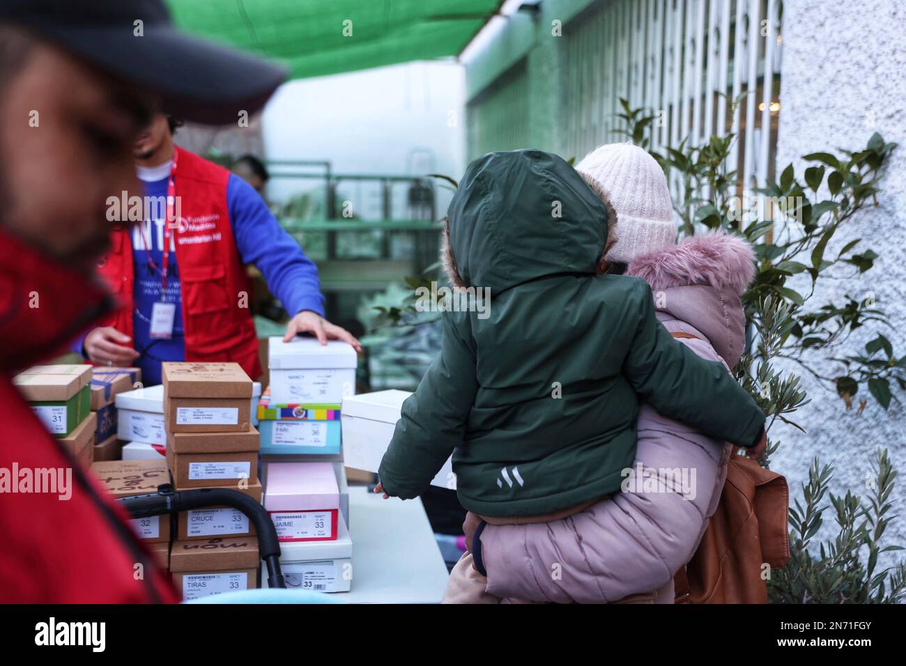A woman with a child in her arms receives winter clothes and shoes that ...