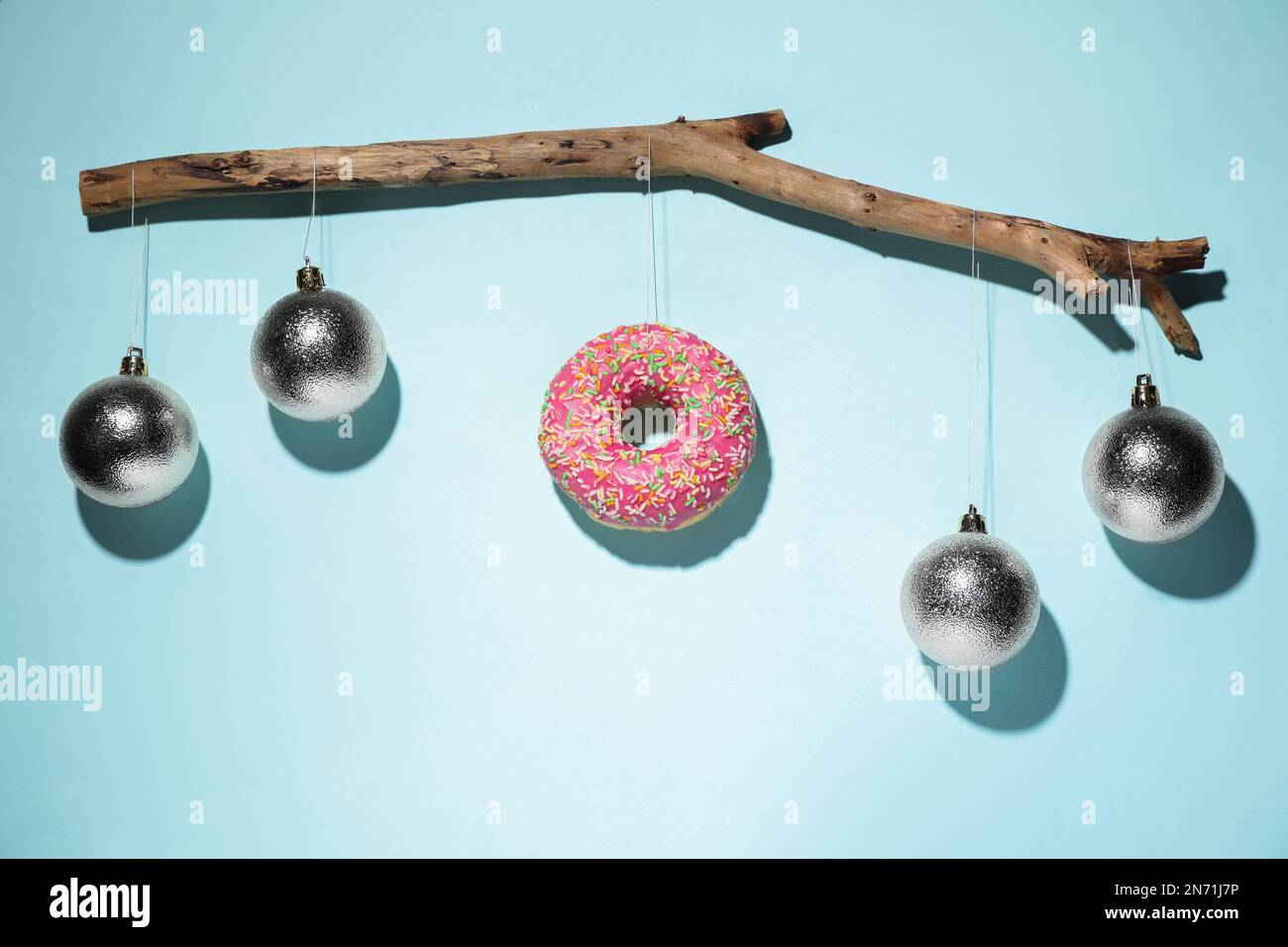 Silver baubles and donut hanging on tree branch against light blue ...