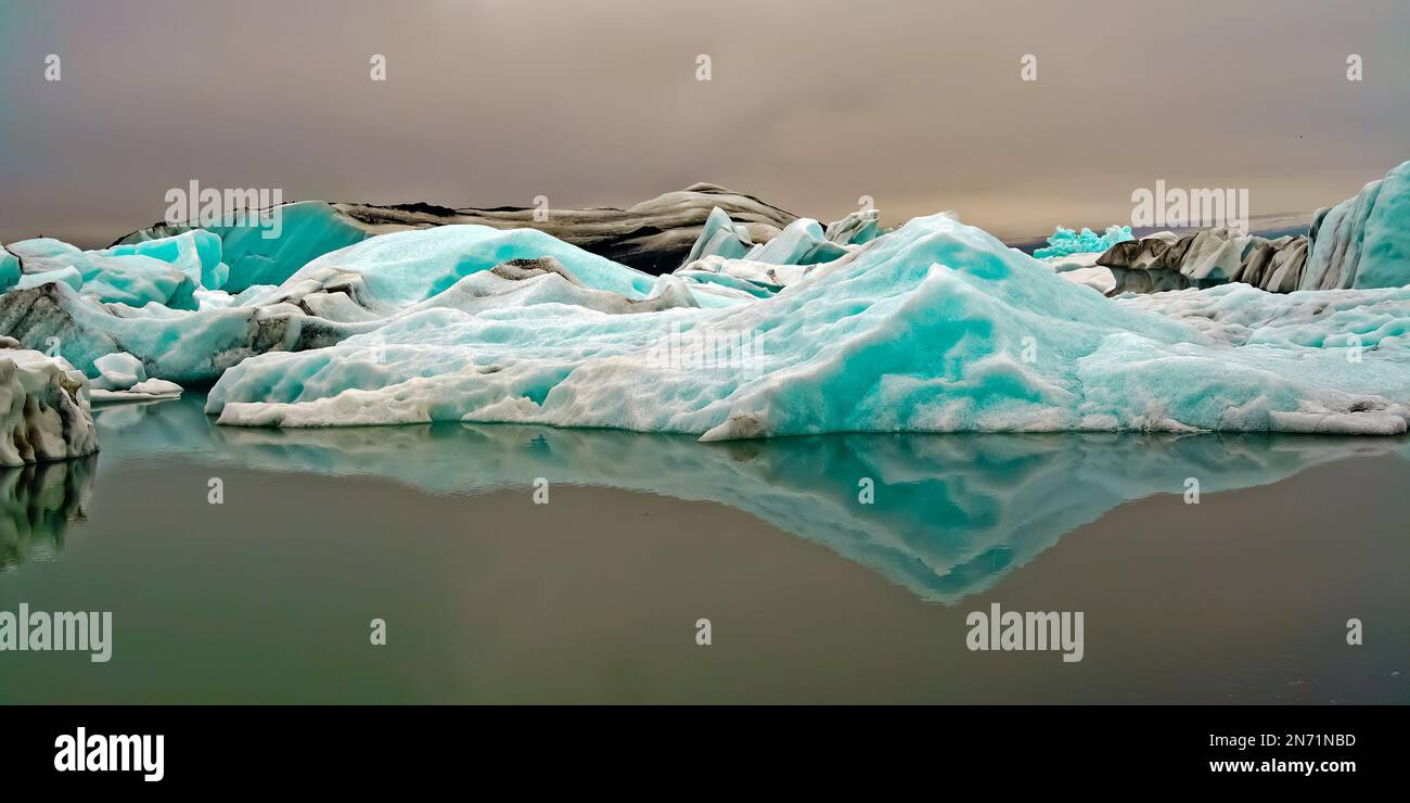 Reflections of crystal blue and white icerberg floes in black dark glassy mirror smooth water in ...
