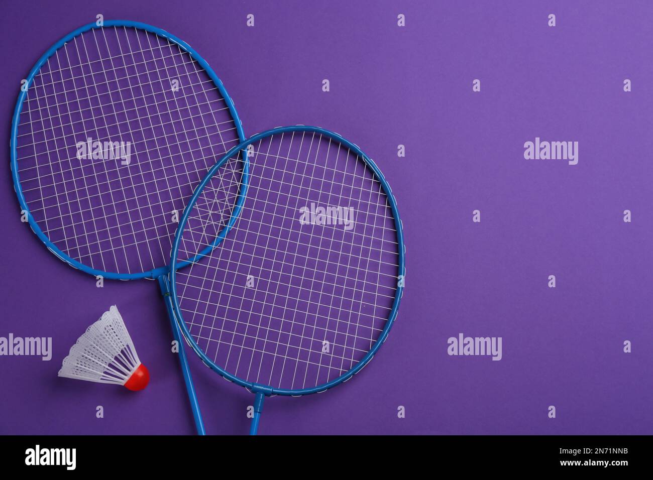 Badminton rackets and shuttlecock on purple background, flat lay. Space ...