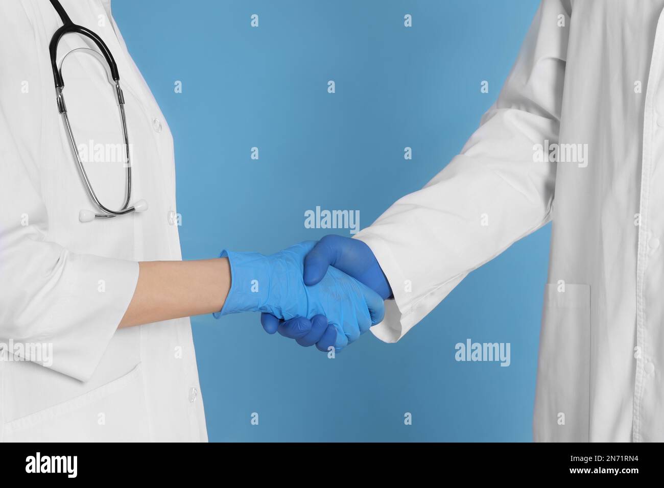 Doctors shaking hands on light blue background, closeup Stock Photo - Alamy
