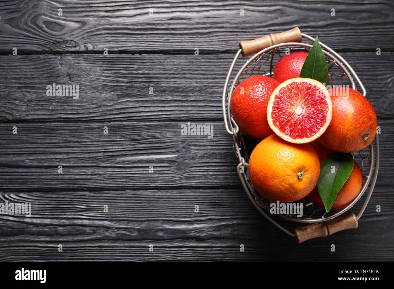 Whole and cut red oranges on black wooden table, top view. Space for ...