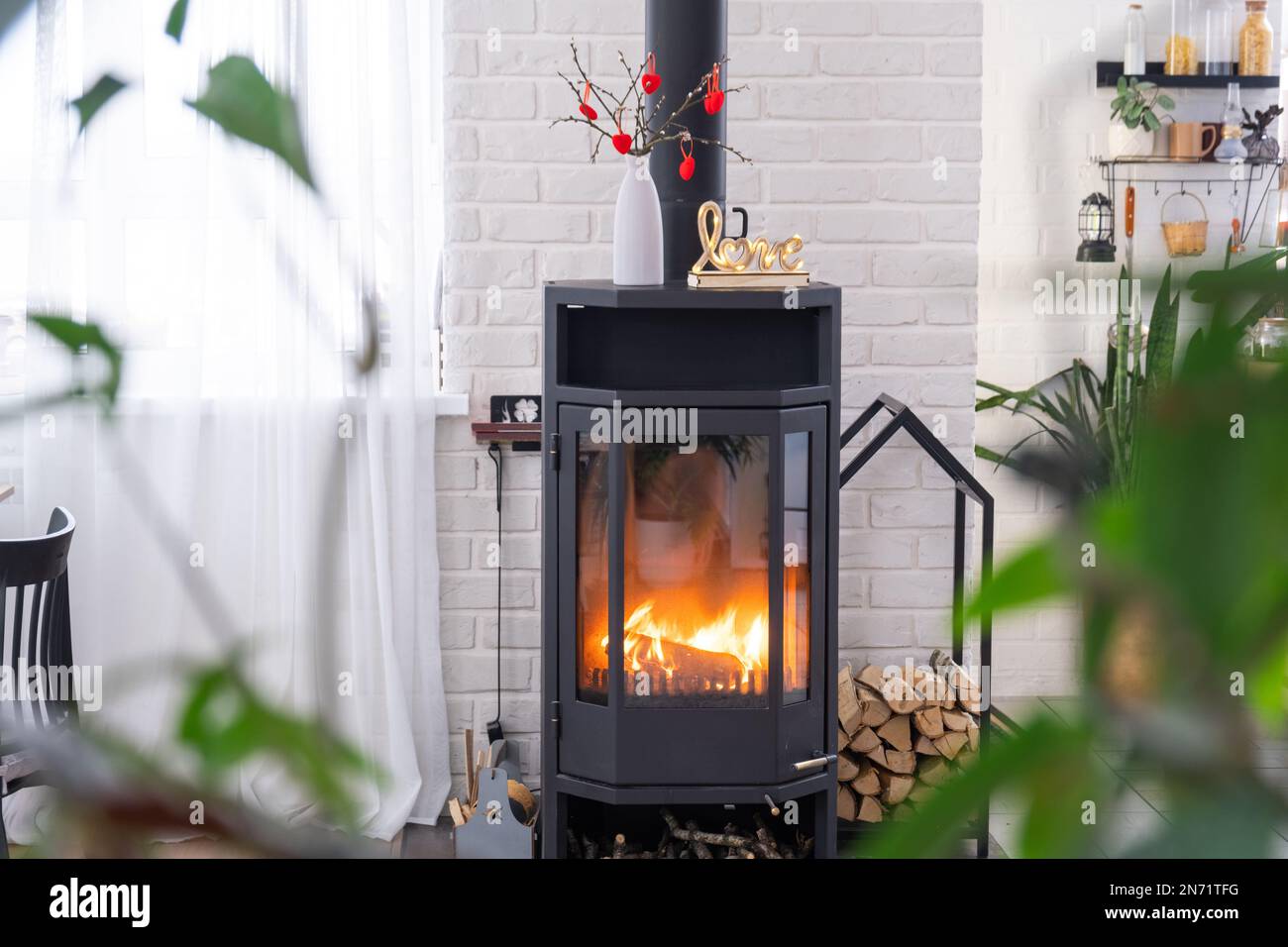 Valentine decor near fireplace stove with fire and firewood. Cozy home ...