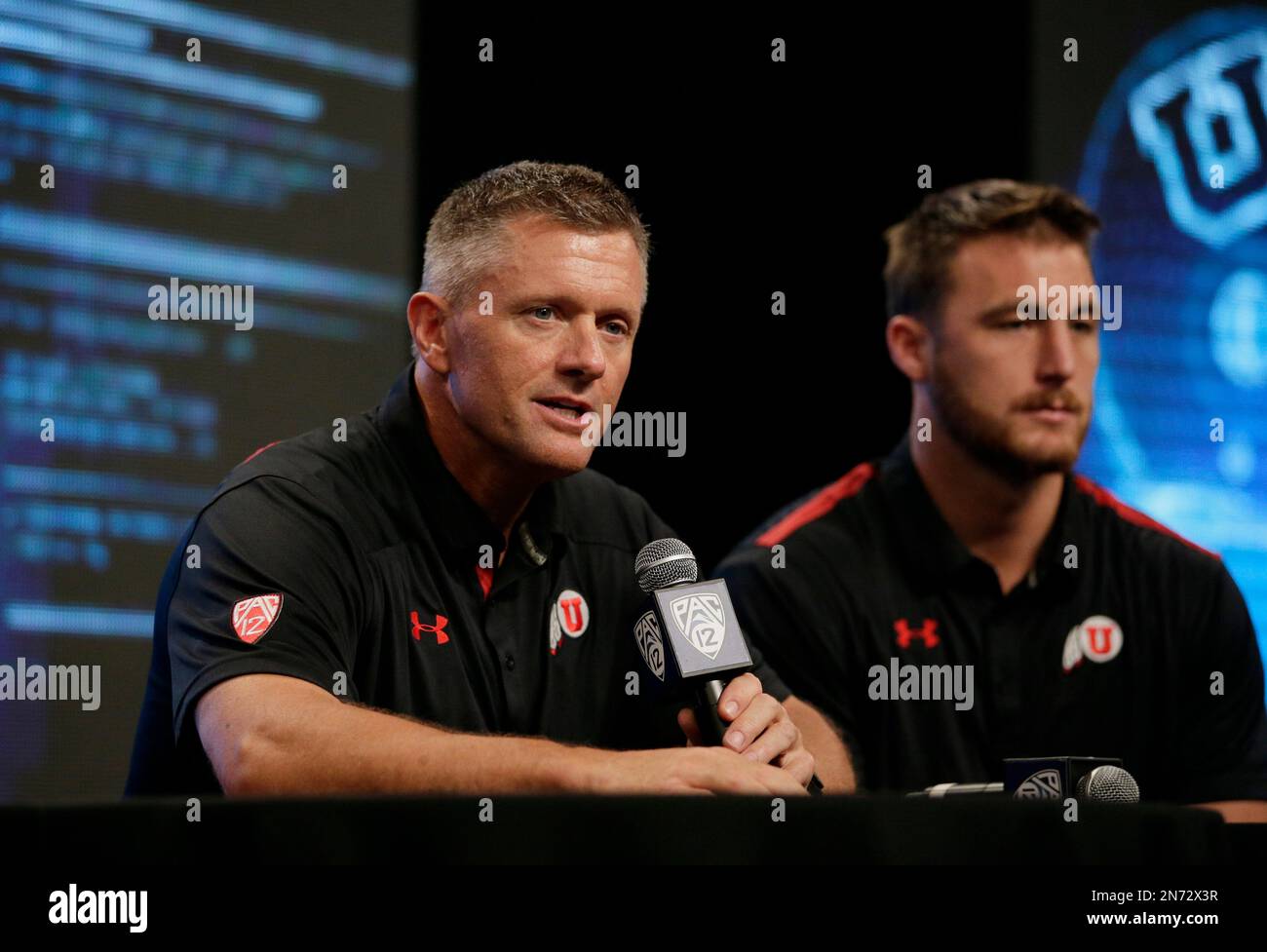Utah head coach Kyle Whittingham, right, talks to the media as he is ...