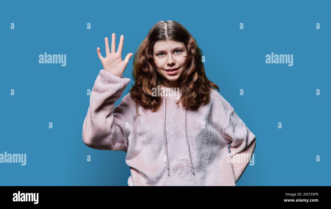 Portrait of smiling child schoolgirl waving hand on blue studio ...