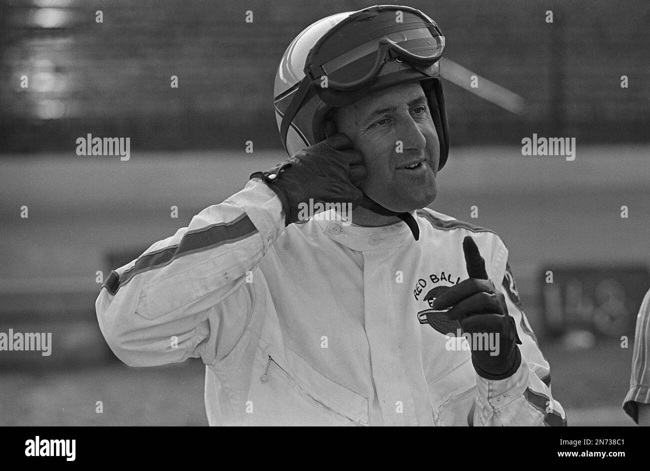 Race driver Eddie Sachs, holds his helmet from his ear with one hand ...