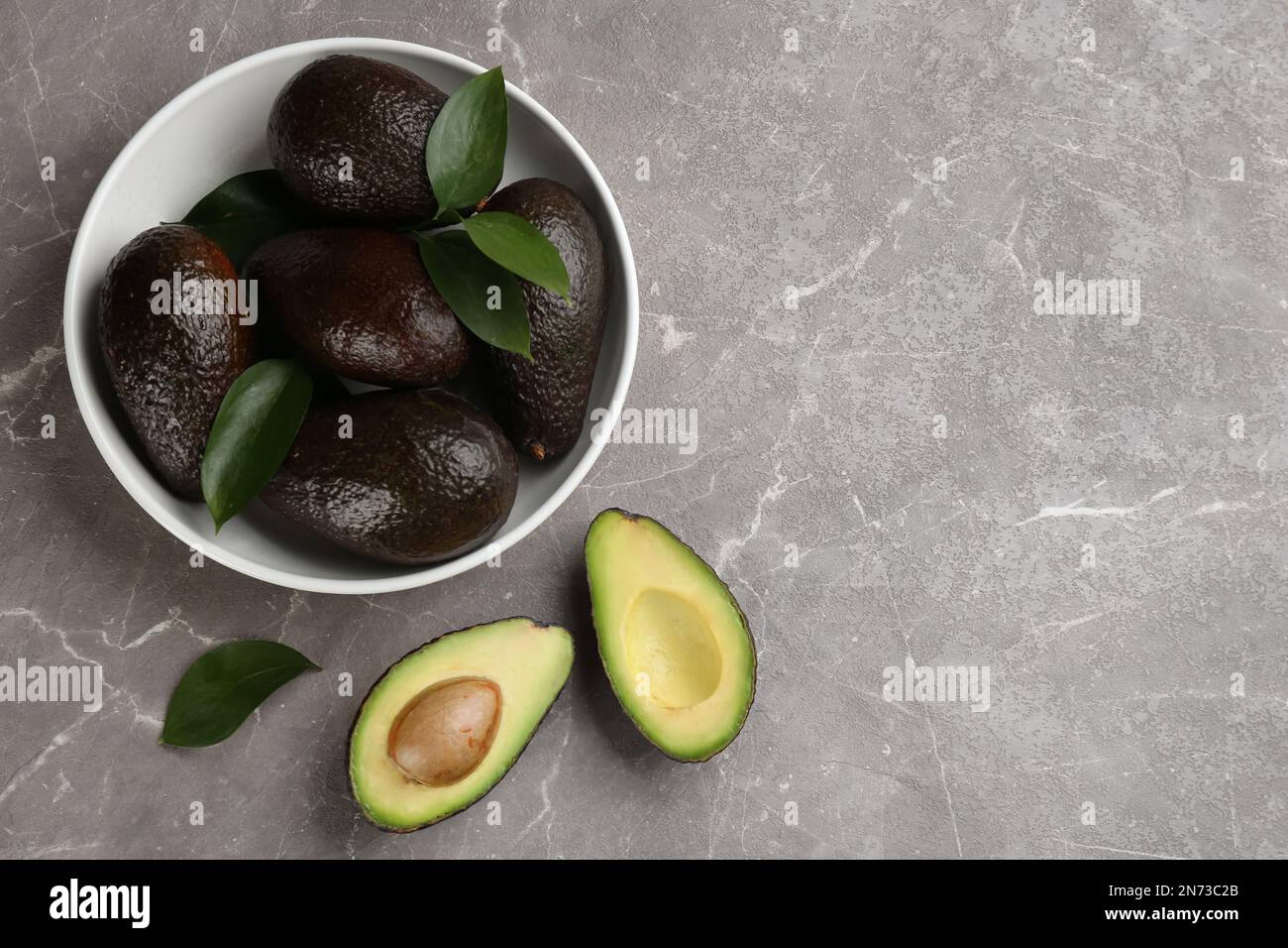 Whole and cut avocados on grey marble table, flat lay. Space for text ...