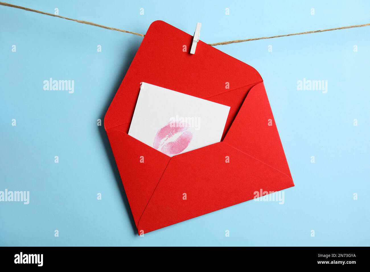 Red envelope and card with lip print hanging on twine against light ...