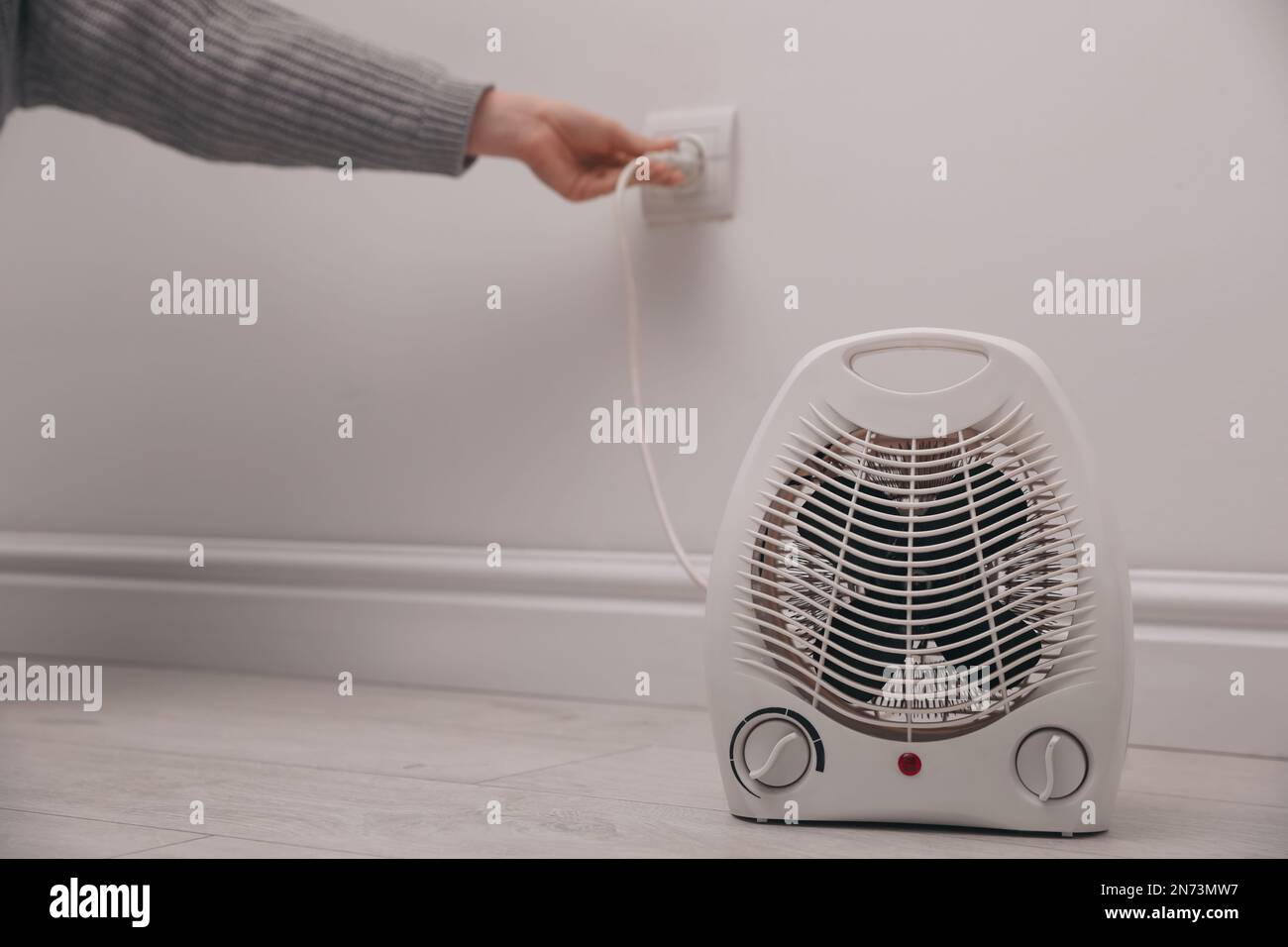 Woman plug in modern electric fan heater indoors, focus on device ...