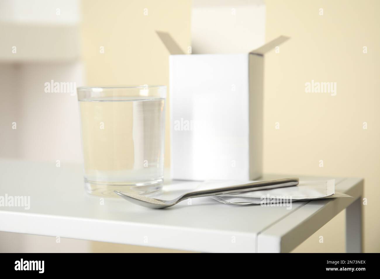 Medicine sachets, glass of water and spoon on white table Stock Photo ...
