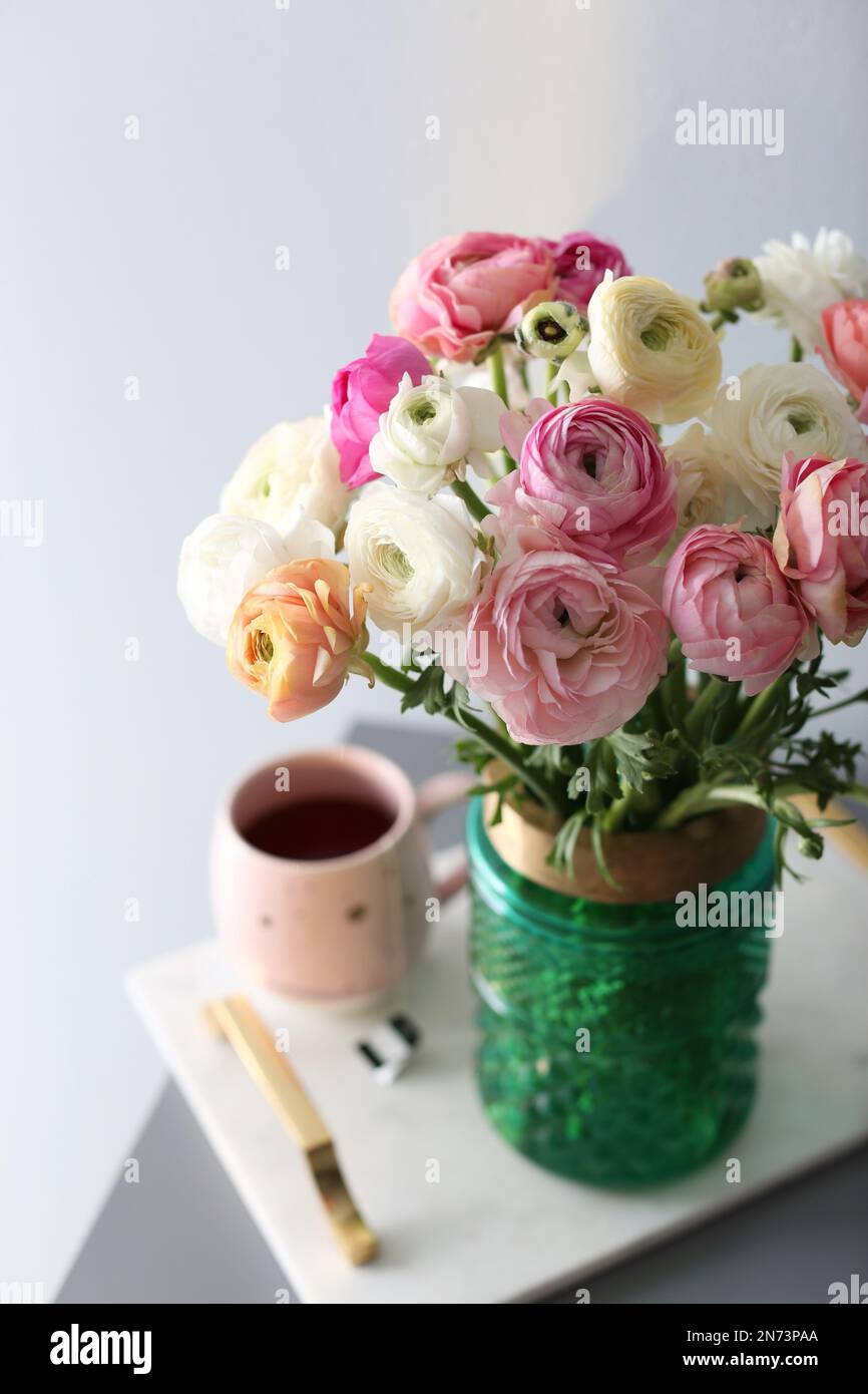 Bouquet of beautiful ranunculuses and tea on table near light grey wall ...