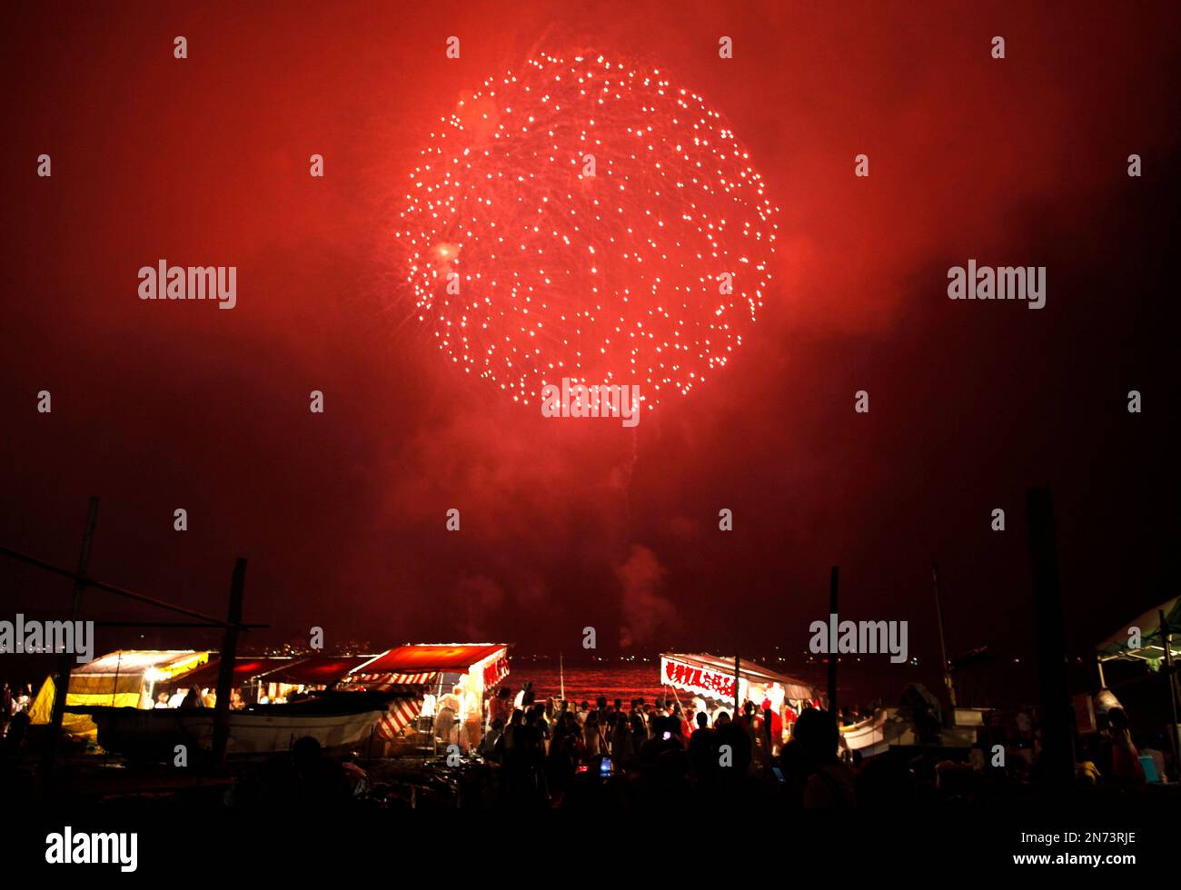 Firework explodes over sidewalk stalls on a beach during a summer ...