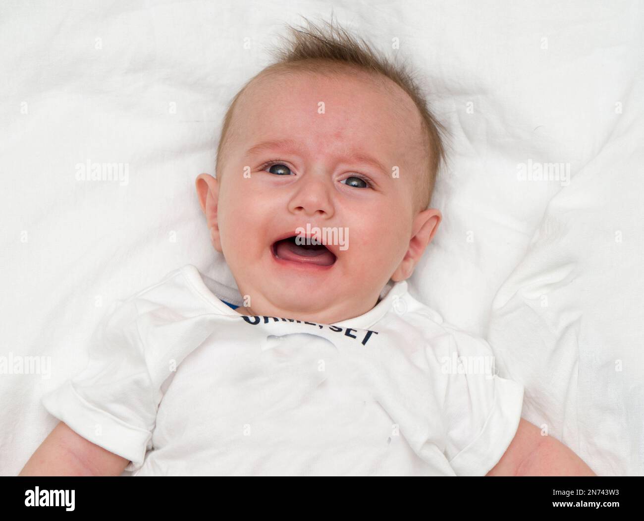 Crying baby lies on a white fluffy background Stock Photo - Alamy