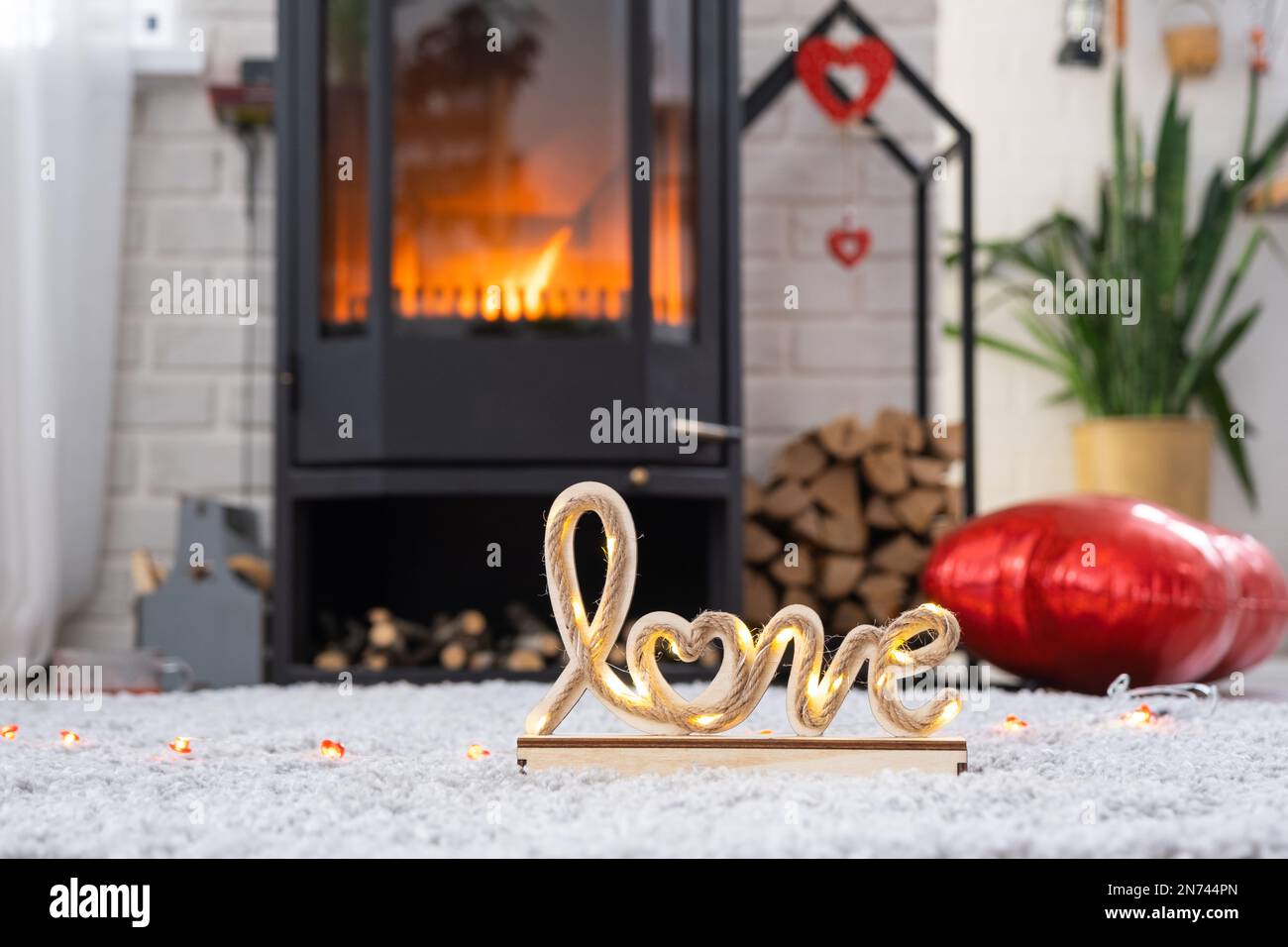 Valentine decor near fireplace stove with fire and firewood. Cozy home ...
