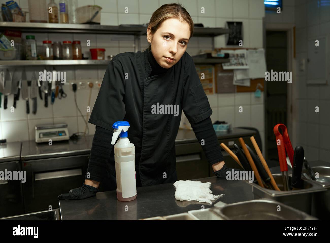 Tired kitchen worker stands against background of kitchen utensils and ...