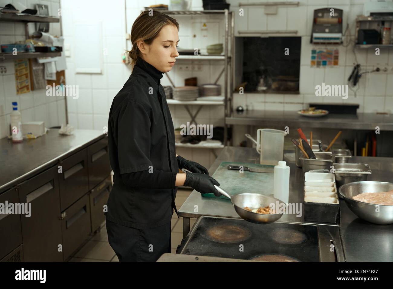 Young chef cooks meat in frying pan, woman in overalls Stock Photo - Alamy