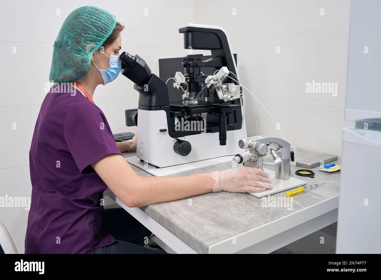 Woman embryologist under microscope carries out the fertilization of ...