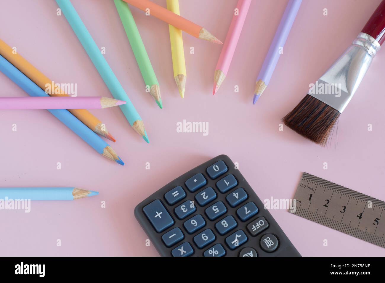 Pastel colored pencils with a brush and a calculator, top view on pink ...
