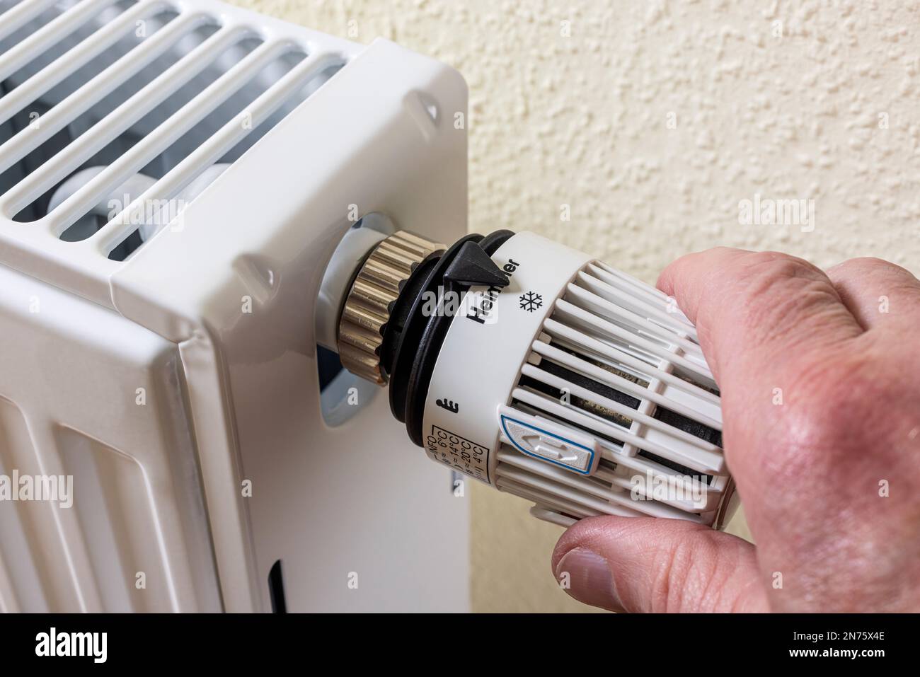 Male hand reduces the room temperature on the radiator thermostat hi ...