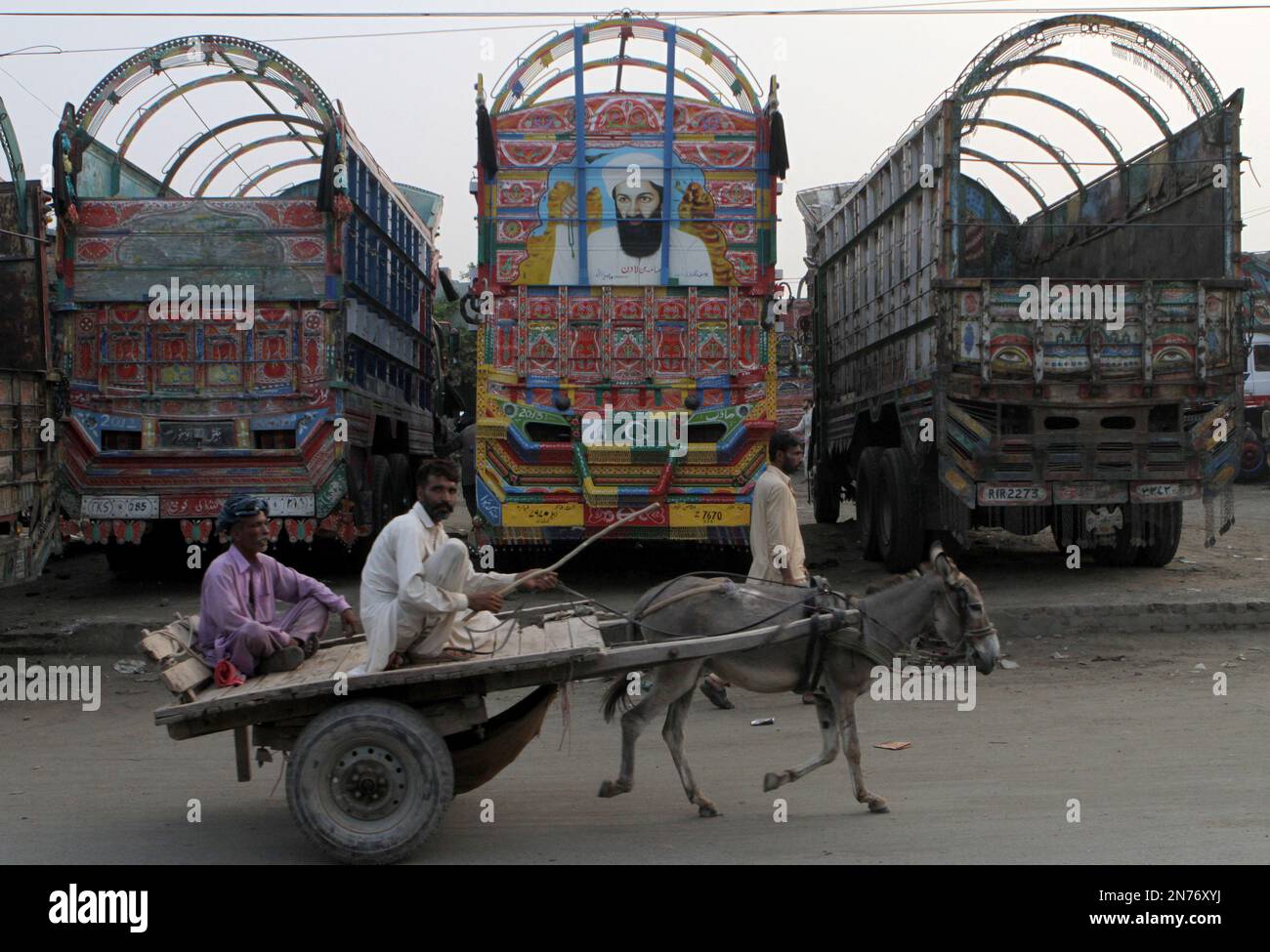 Pakistani donkey cart riders drive past a portrait of al-Qaida leader ...