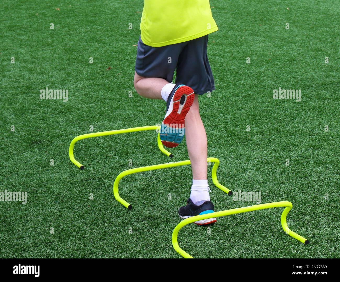 Young teenage boy jumping over yellow mini hurdels on a turf field ...