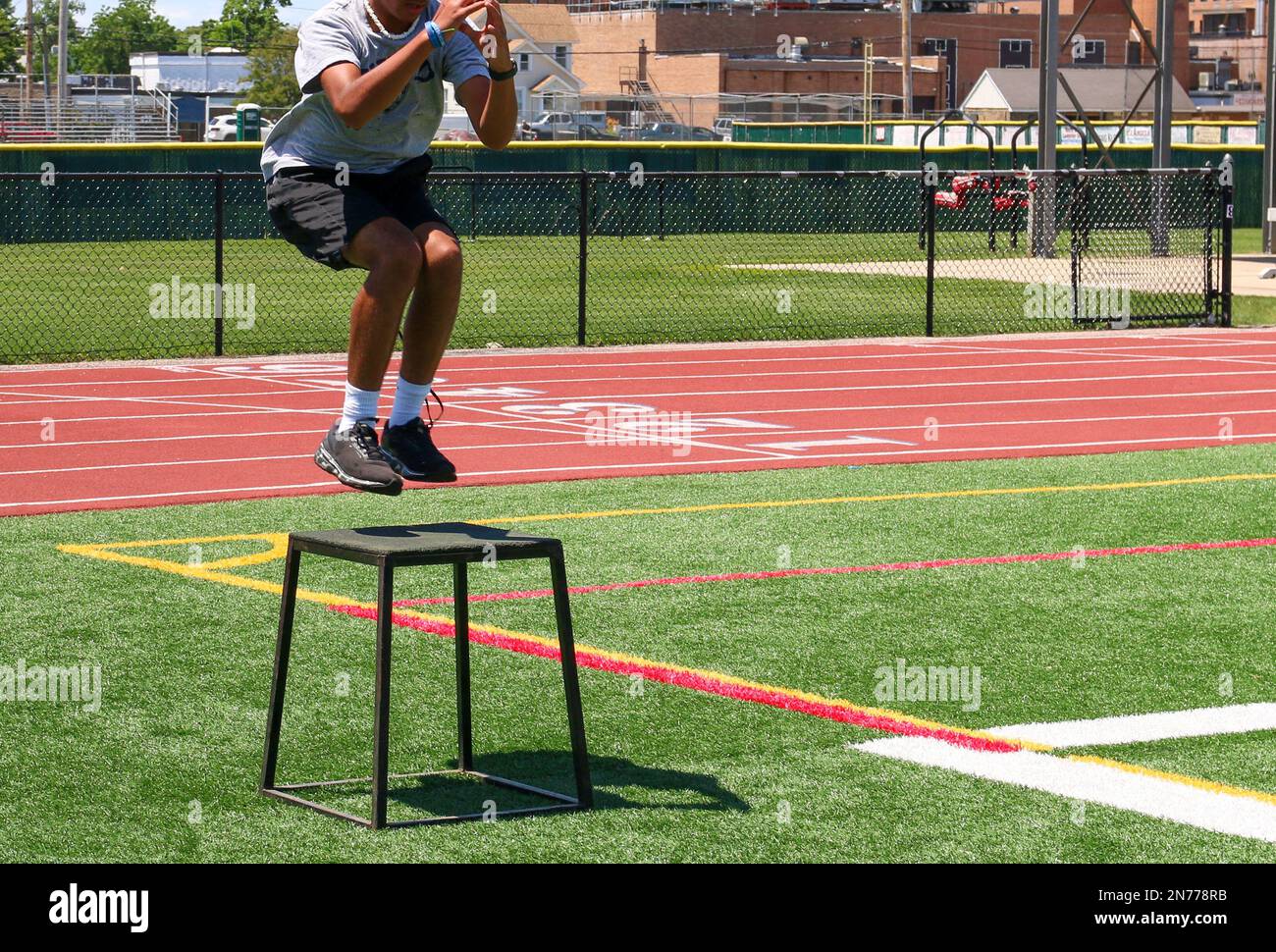 A high school boy jumping onto a plyo box at track and field summer ...