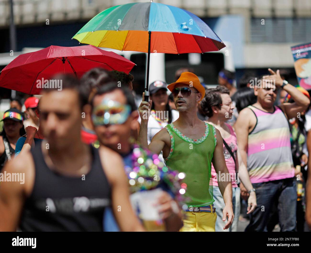 A participant shades himself with a rainbow colored umbrella during a ...