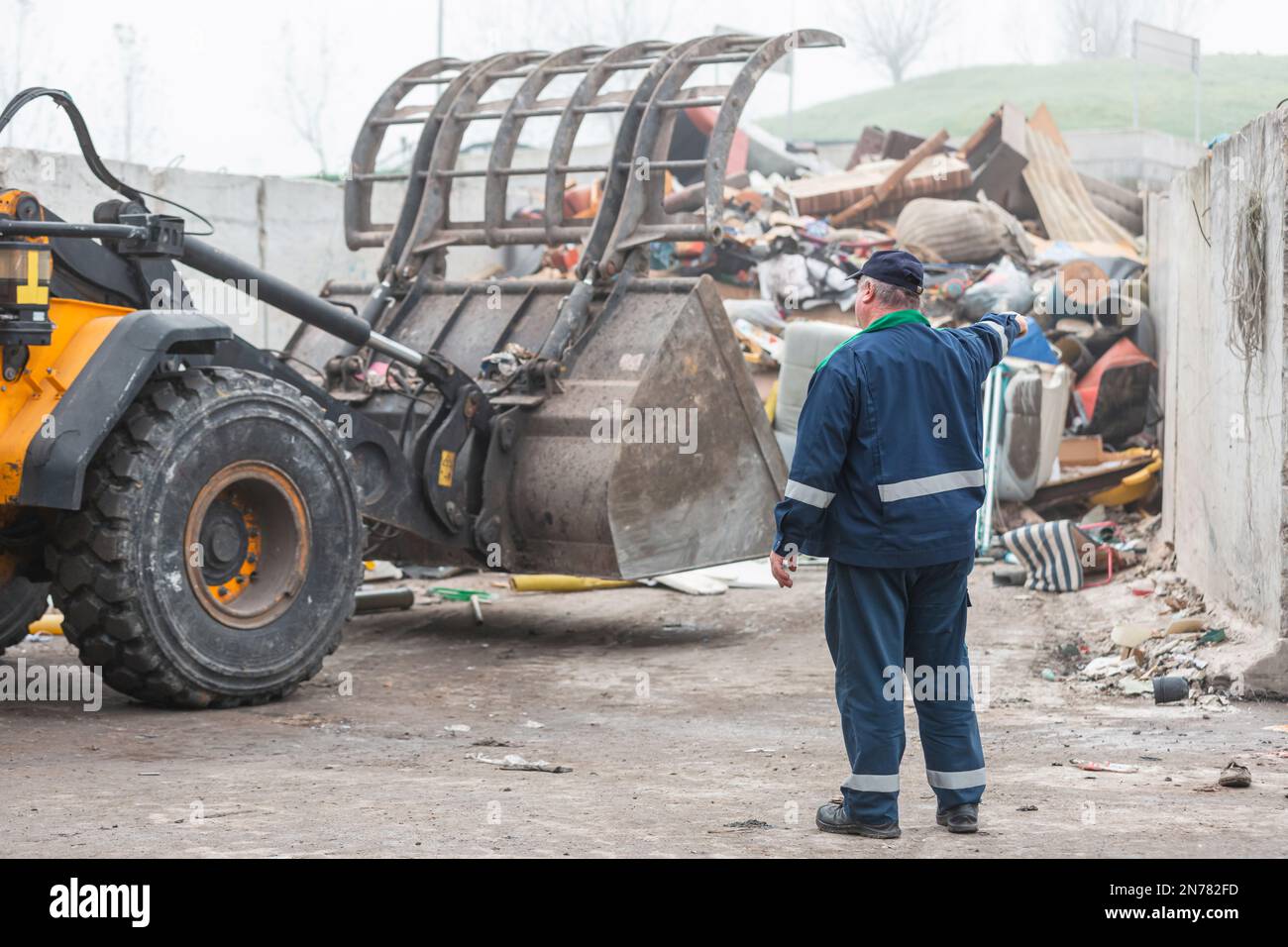 Male worker pointing on wheel loader and the garbage heap at a landfill ...