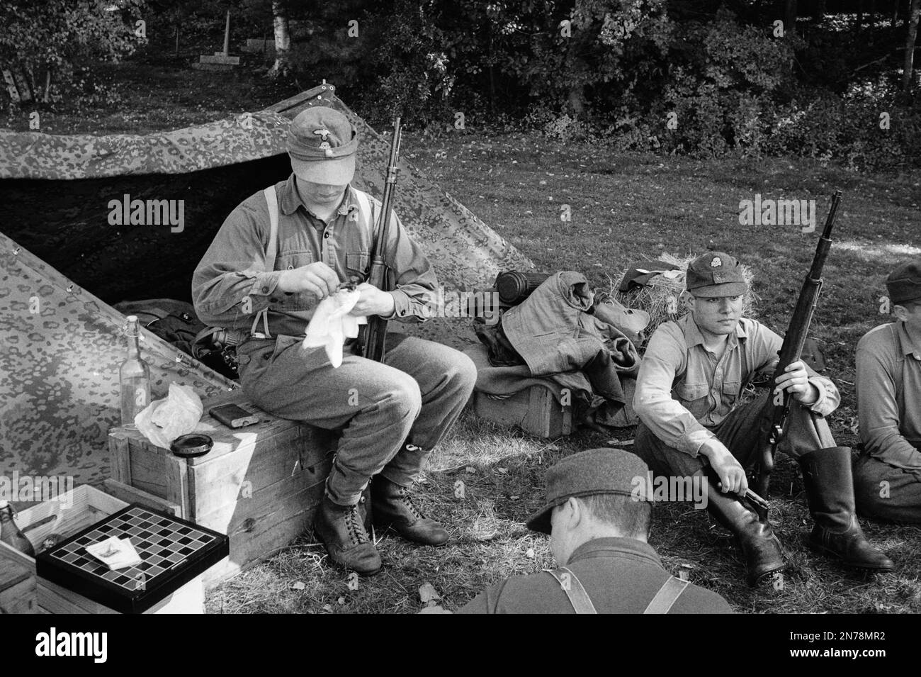 Young WWII German soldier sitting around a pup tent, one oiling his gun ...