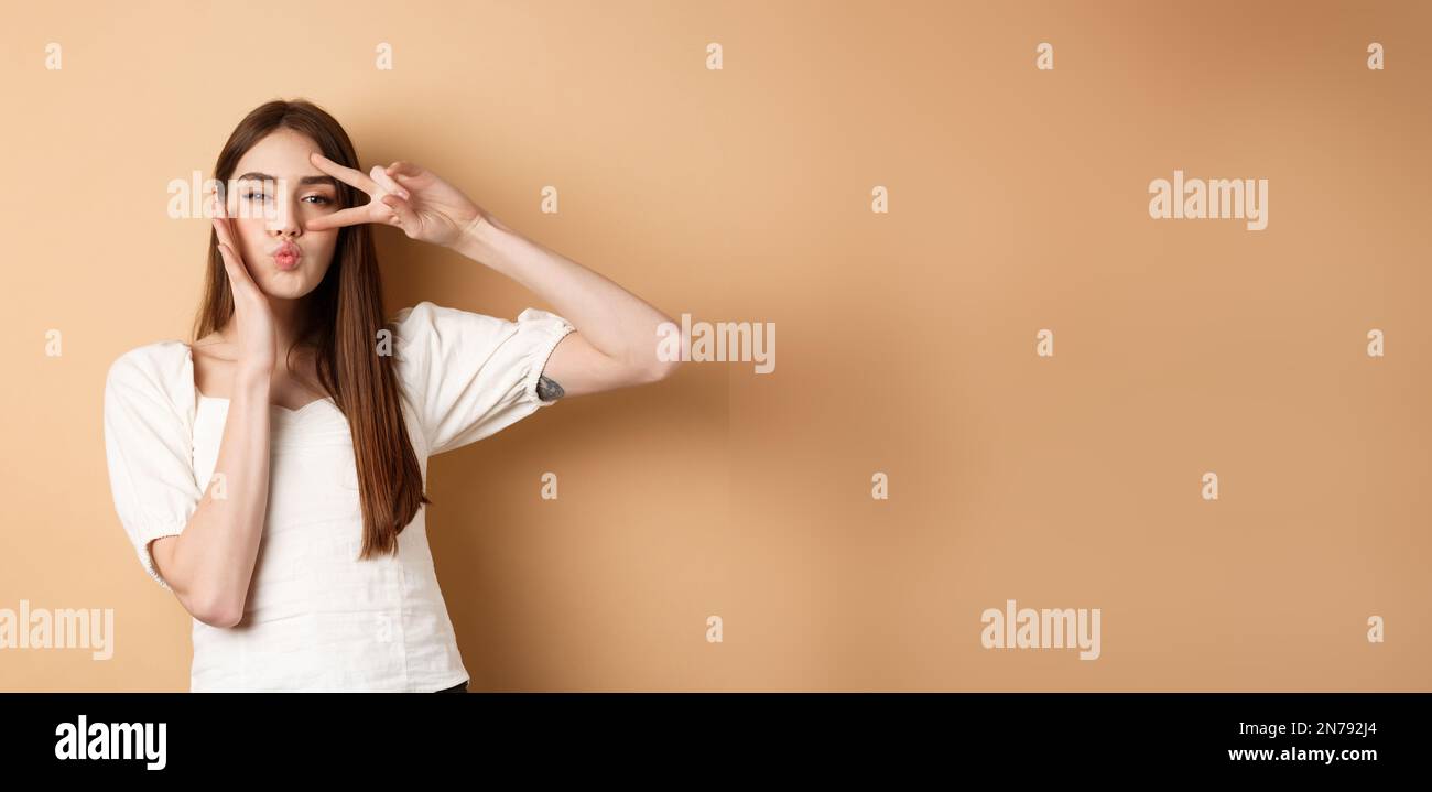 Cute woman showing v-sign and pucker lips for kiss, touching face with ...