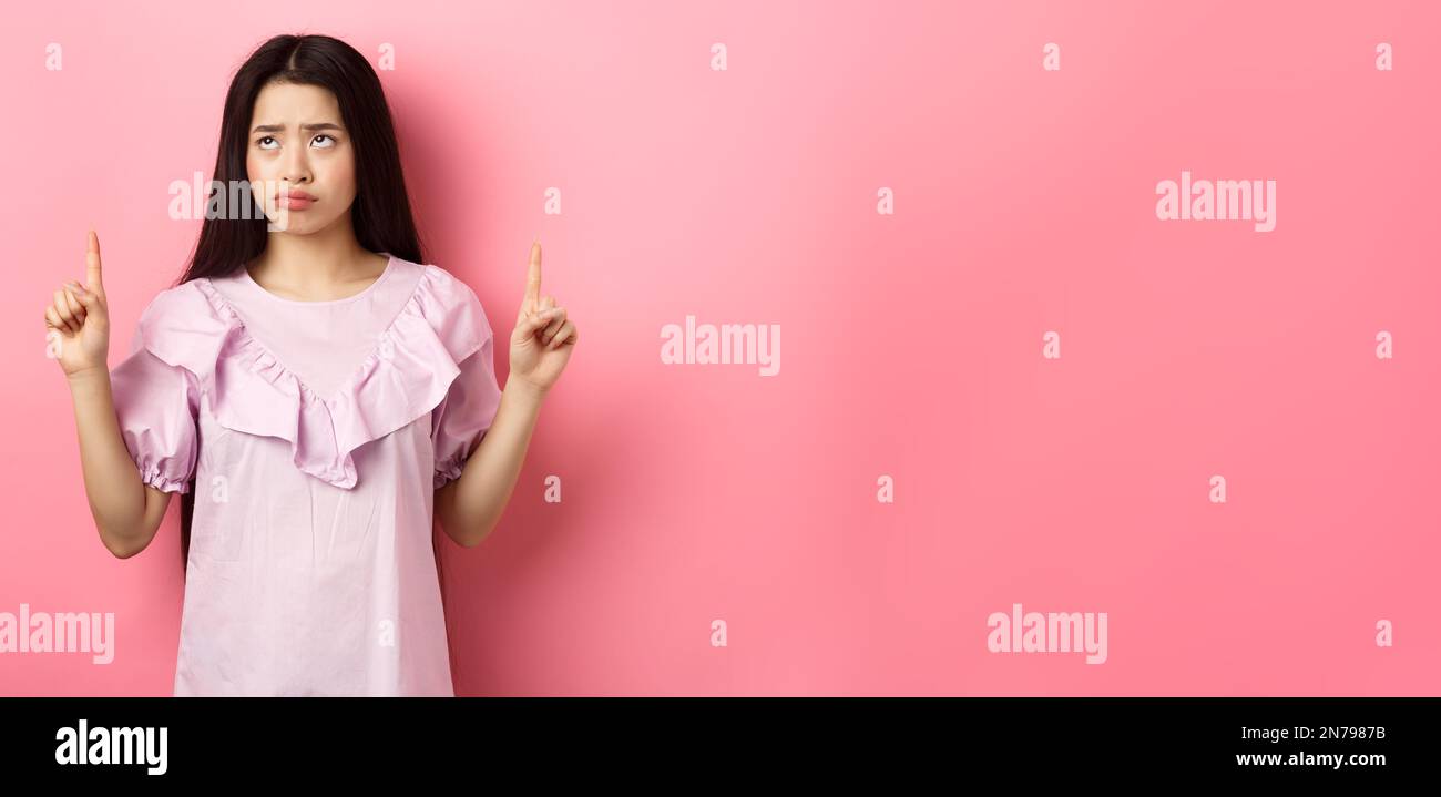 Sad pitiful asian girl sulking, pointing and looking up with ...