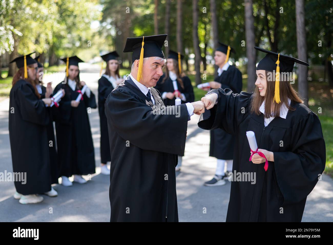 A group of graduates in robes outdoors. An elderly man and a young ...
